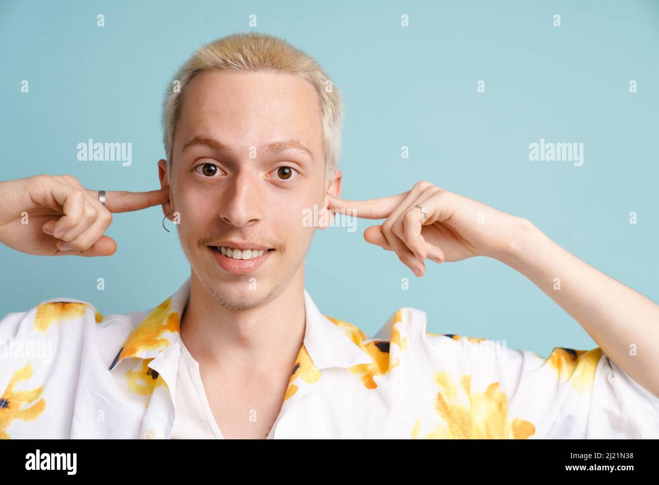 Young blonde man in shirt smiling and plugging his ears isolated over ...