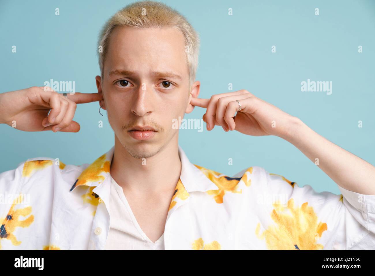 Young blonde man looking at camera while plugging his ears isolated ...