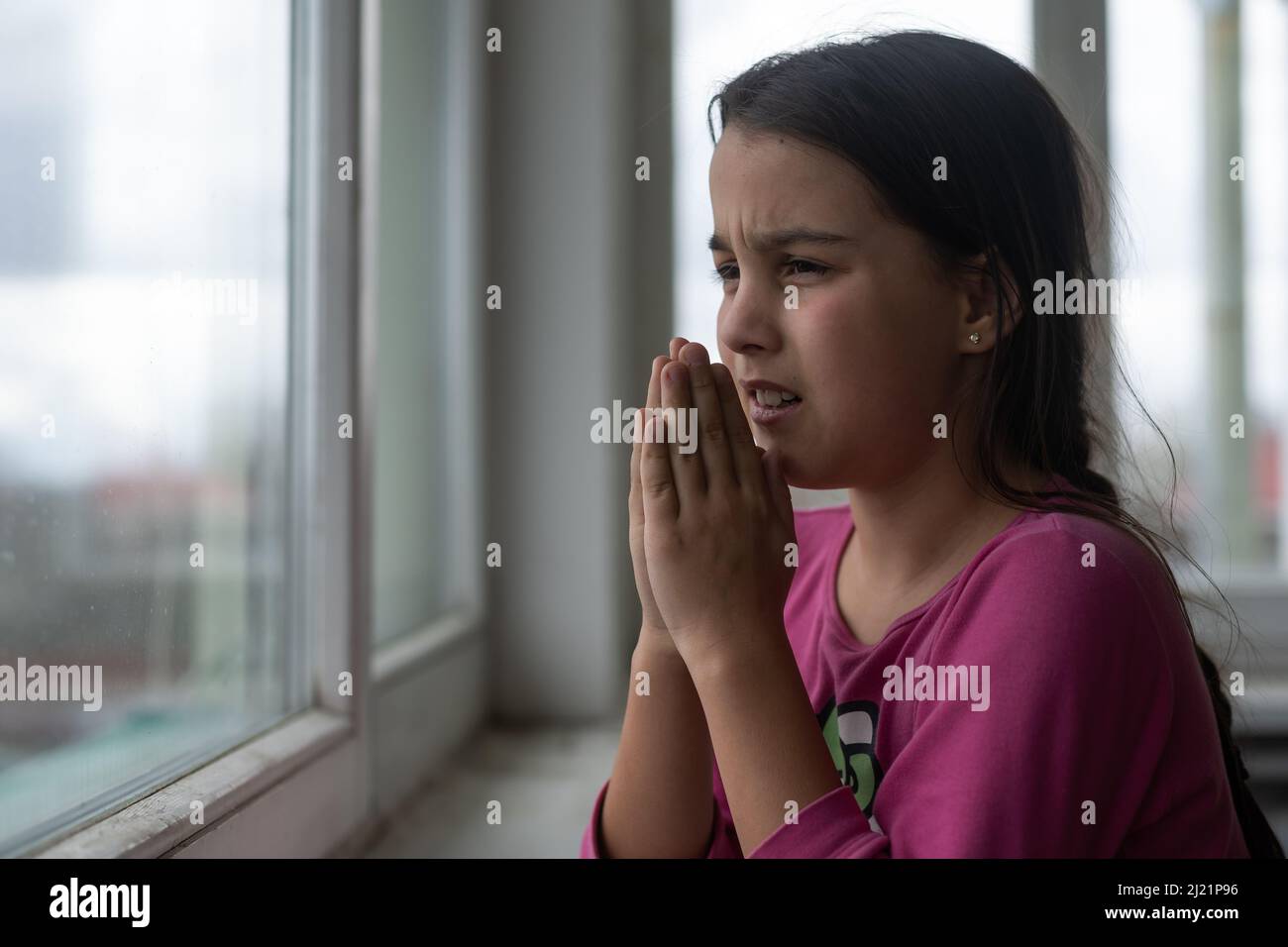 Praying little girl near window Stock Photo - Alamy