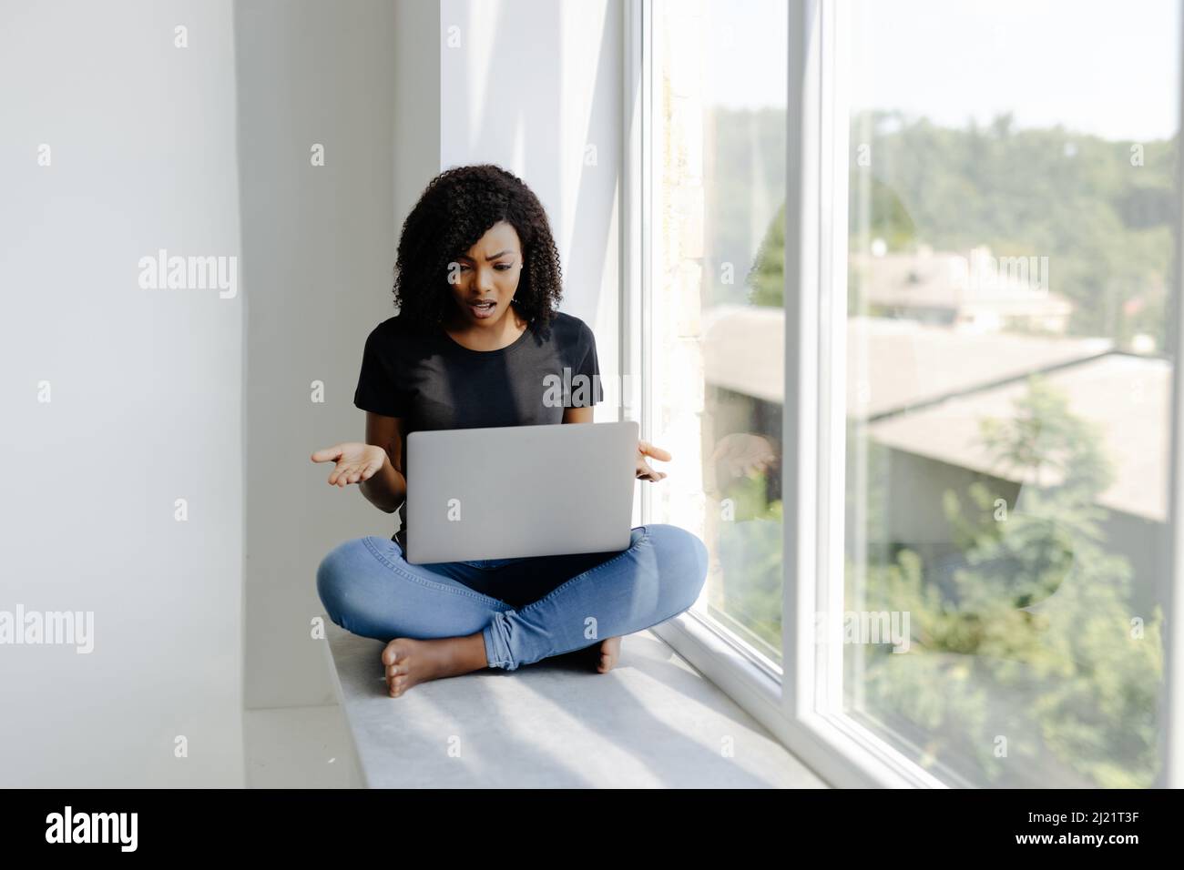 Young african woman confused look at laptop sitting on windowsill at ...