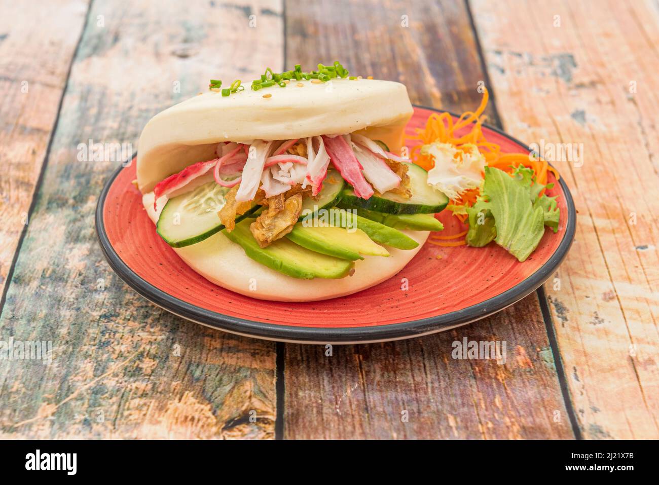 Bao bread sandwich with surimi, avocado, pickles and chives on a red ...