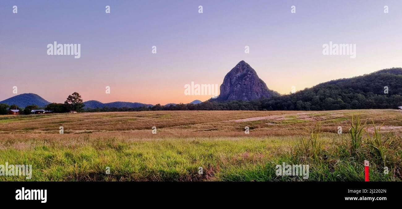 A landscape with field and a small rocky hill in a background of sunset ...