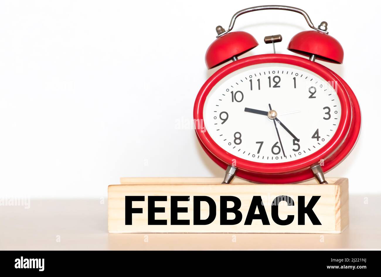 Red alarm clock and TIME FOR FEEDBACK inscription written on natural ...