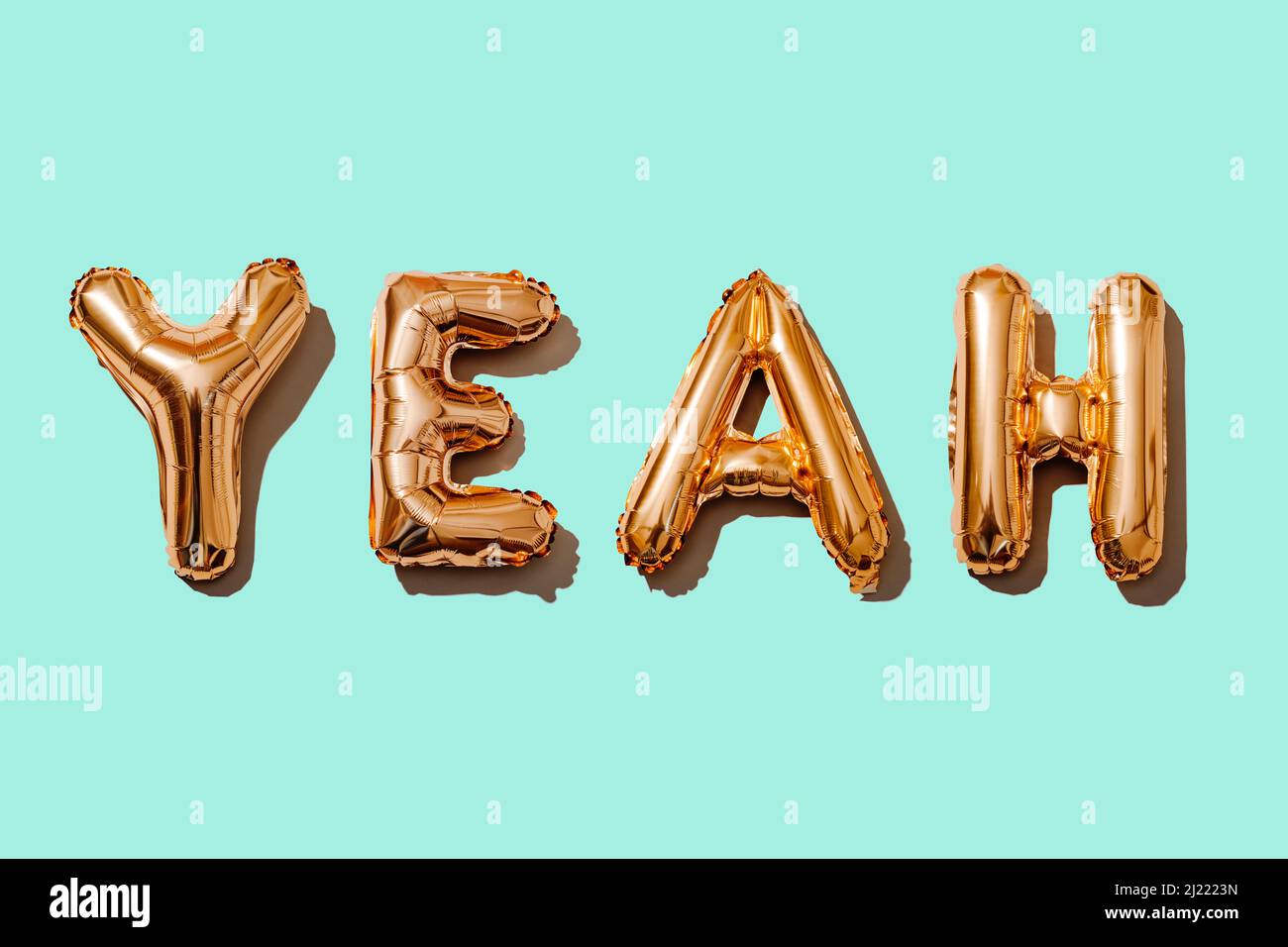 golden letter-shaped balloons forming the word yeah on a blue ...