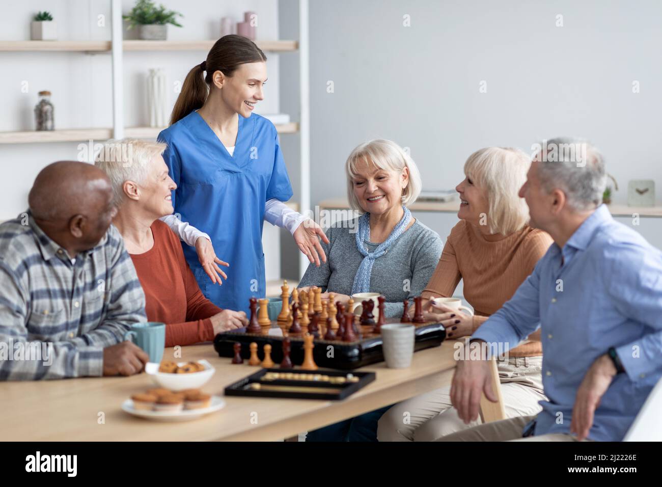 Friendly nurse talking to elderly people playing table games Stock ...