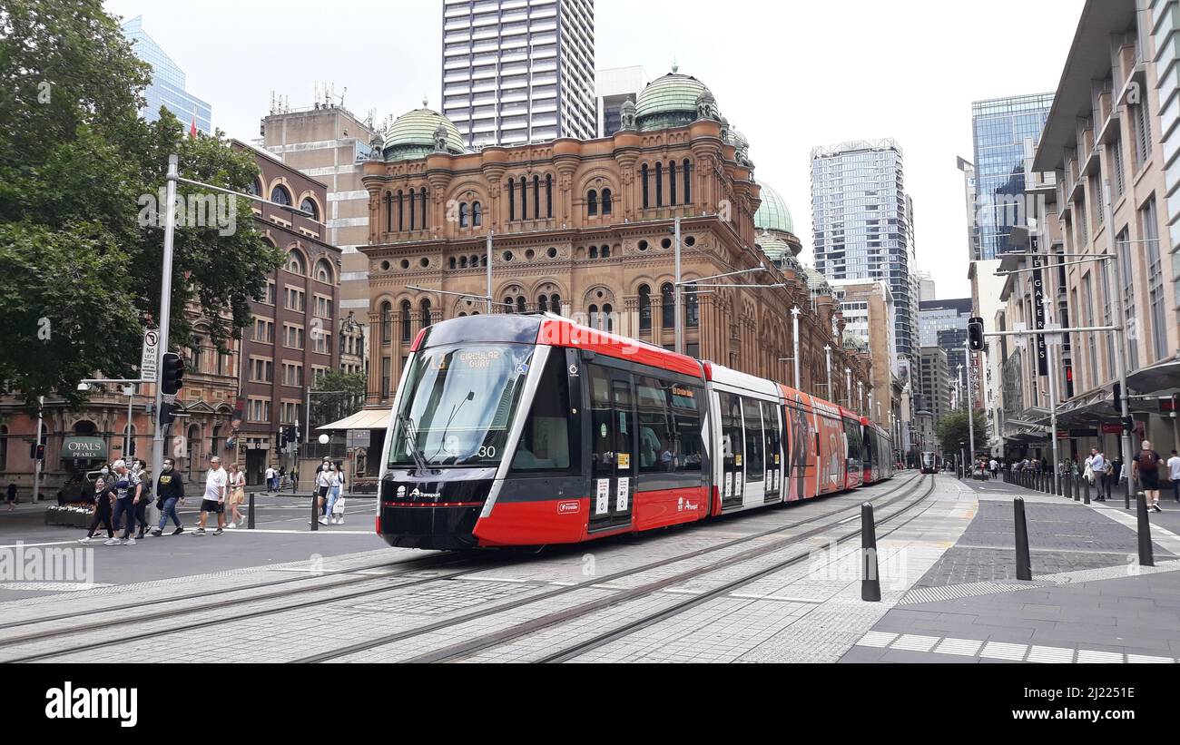 A red tram going through a street with the Queen Victoria Building in ...