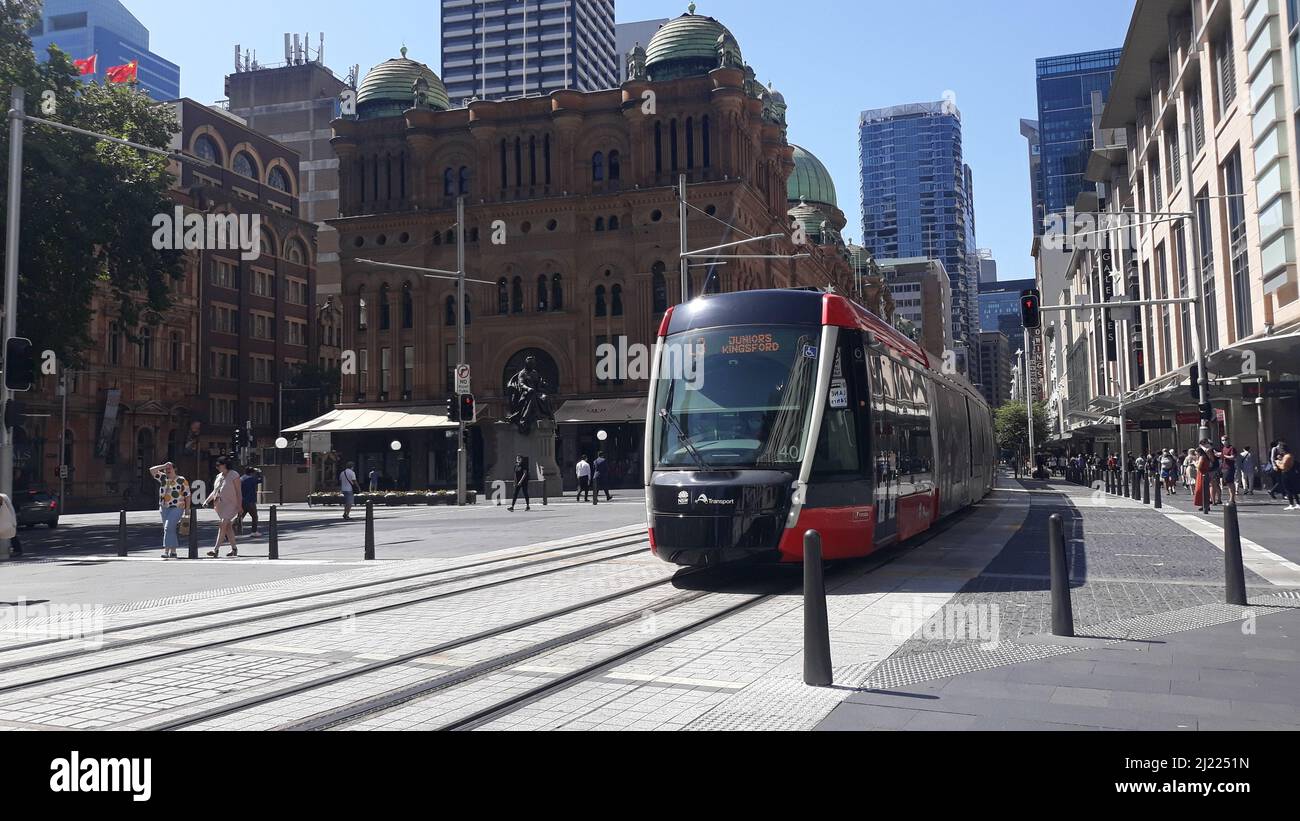 A red tram traveling through a street with the Queen Victoria Building ...