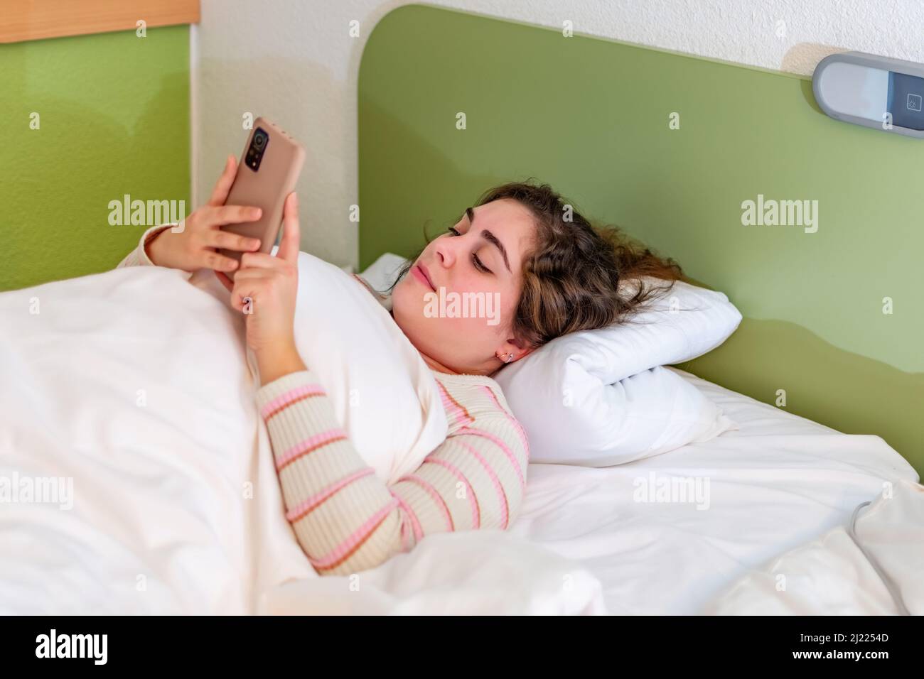 Young woman using phone lying in her bed. Smart phone addiction Stock ...