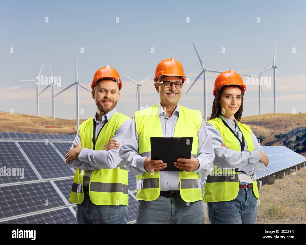 Team of engineers with safety vests on a wind and solar farm smiling at ...