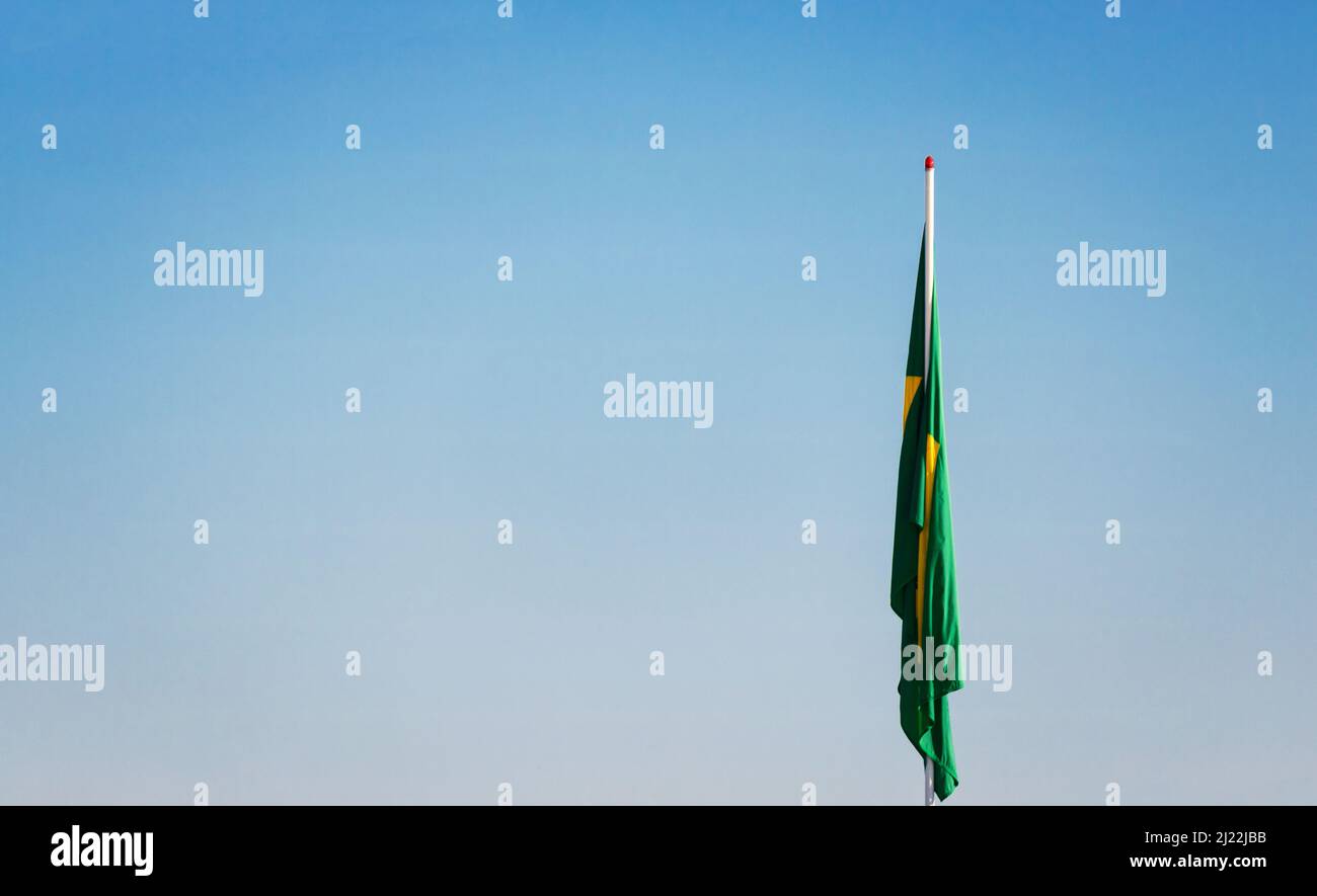 Concept image of a brazilian flag on pole without wind in front of blue ...