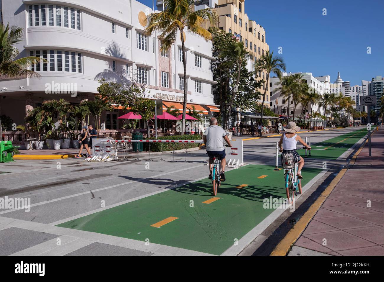A mature Couple rides bicycles past Art deco buildings on Ocean Drive ...