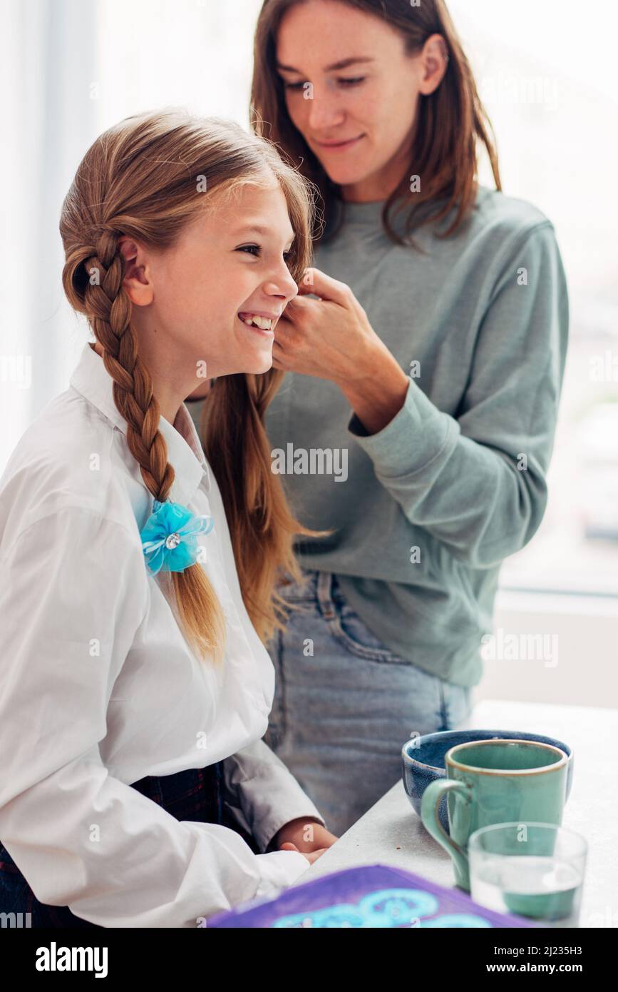 Mother and daughter at breakfast before school in the kitchen braiding ...