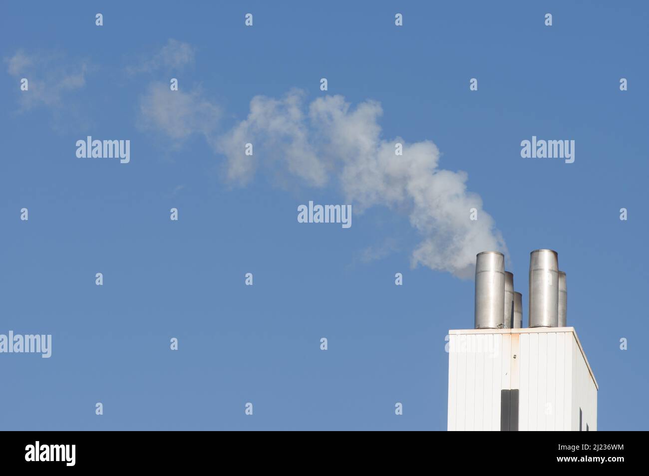 Closeup of a white industrial smokestack with white smoke a clear blue ...