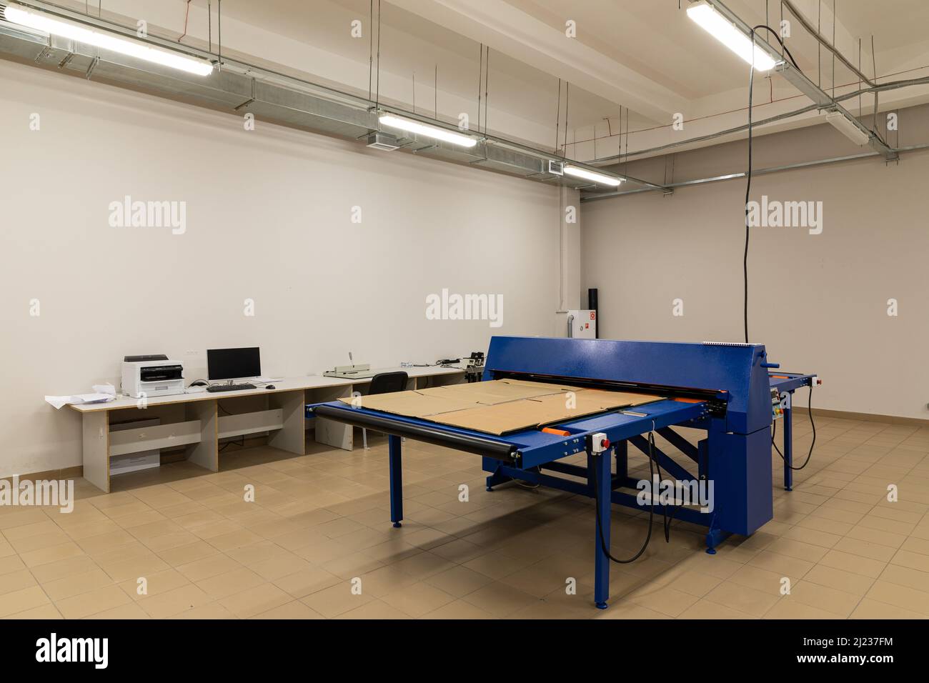 Photo of a blue cardboard cutter in a factory. Production of cardboard ...