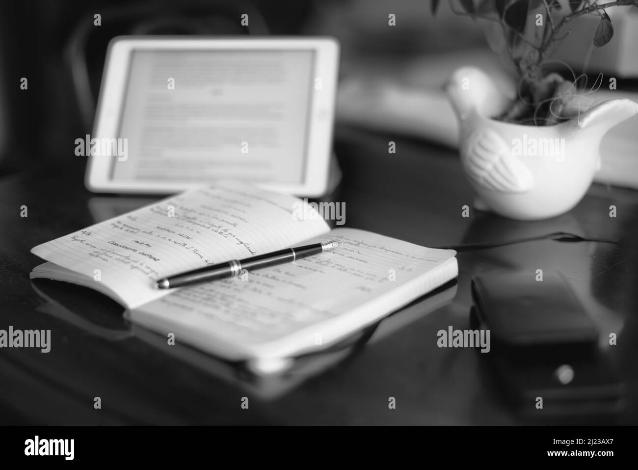 A grayscale shot of office workplace with tablet and notebook on a ...