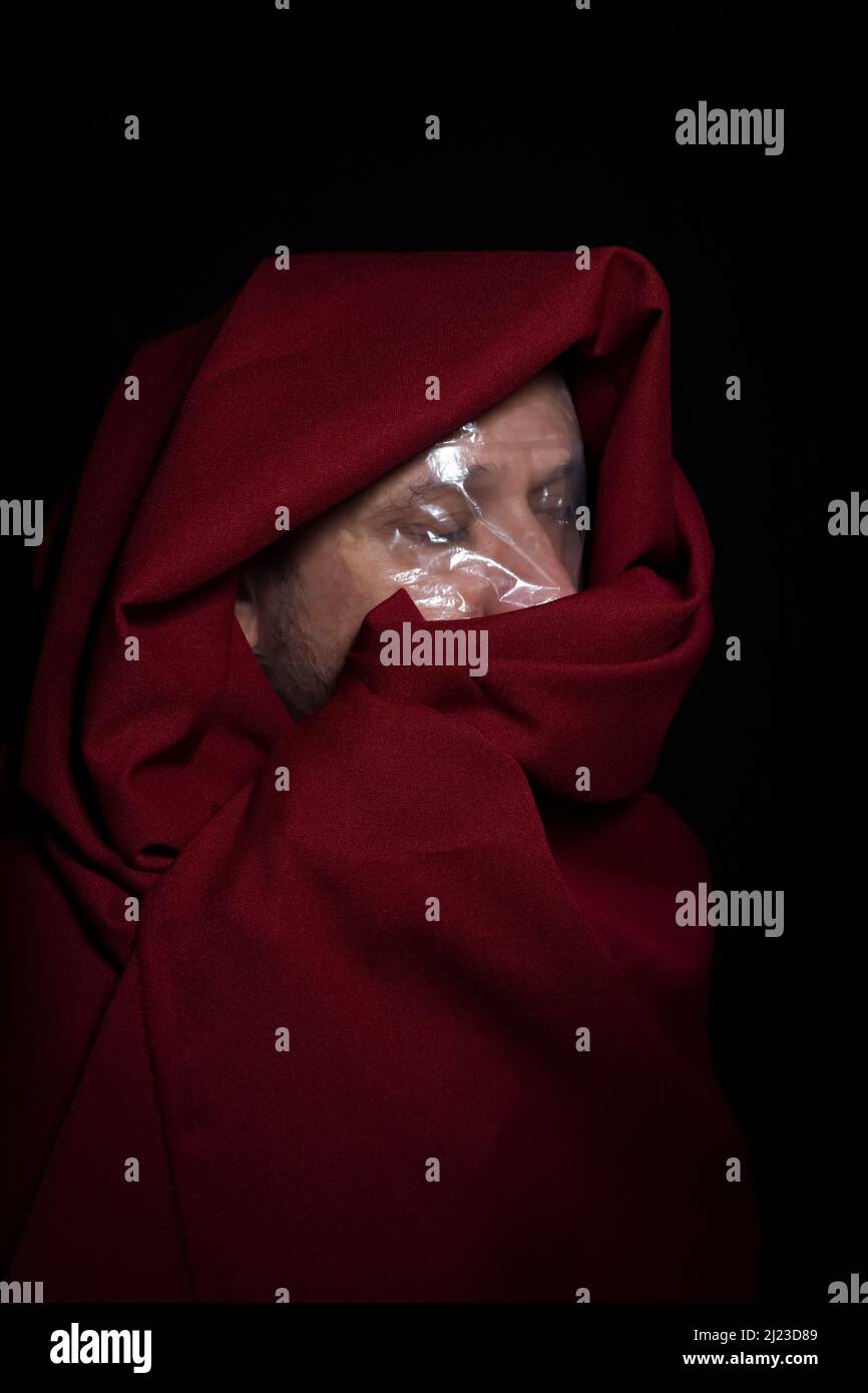Man covered in red cloth with plastic on his face against black ...