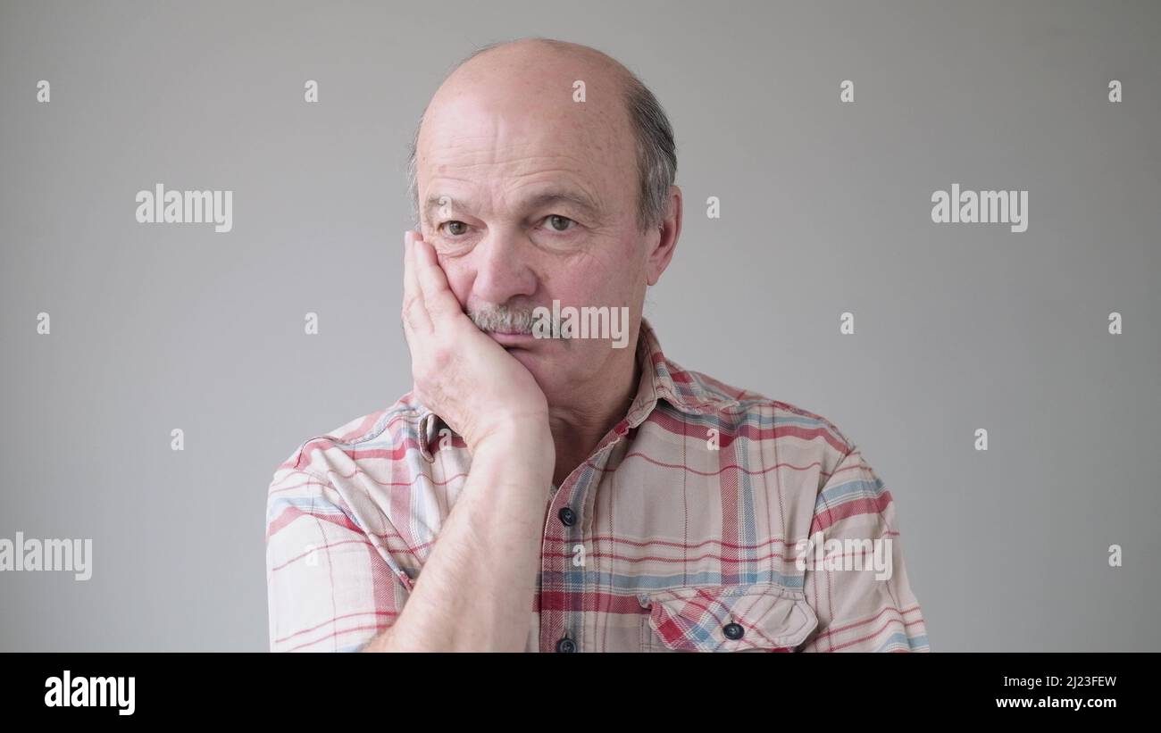 Bored senior hispanic man holding hand on his cheek has gloomy and sad ...