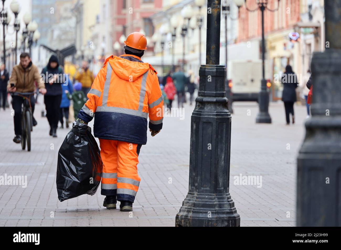 Worker carries a garbage bag down the street on people background ...