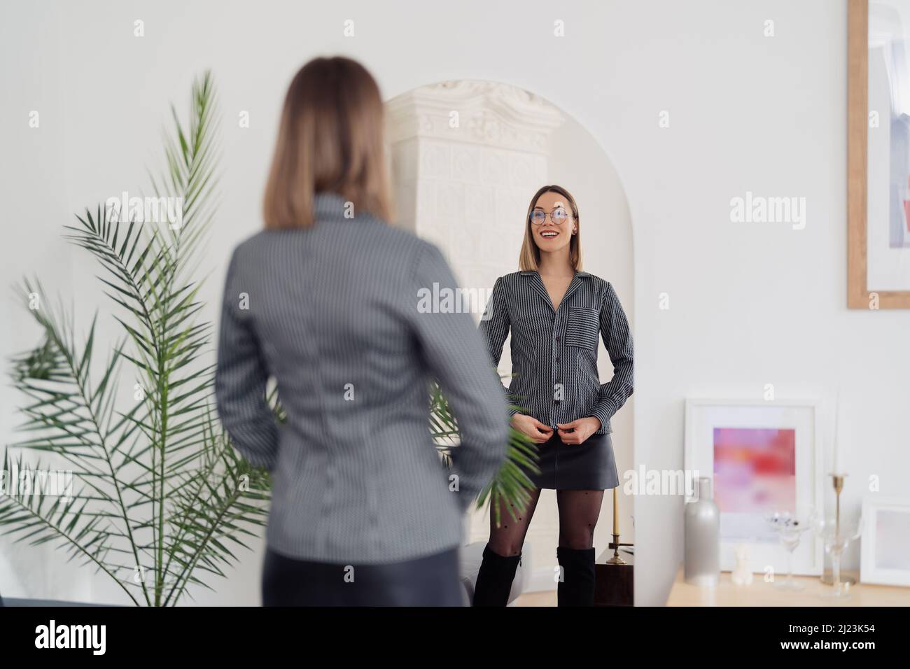 Self-confident Woman looking at her reflection into the mirror indoors ...
