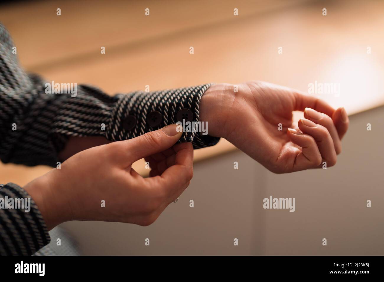 Woman hands buttoning the cuff on the shirt in a soft light. Clothes ...