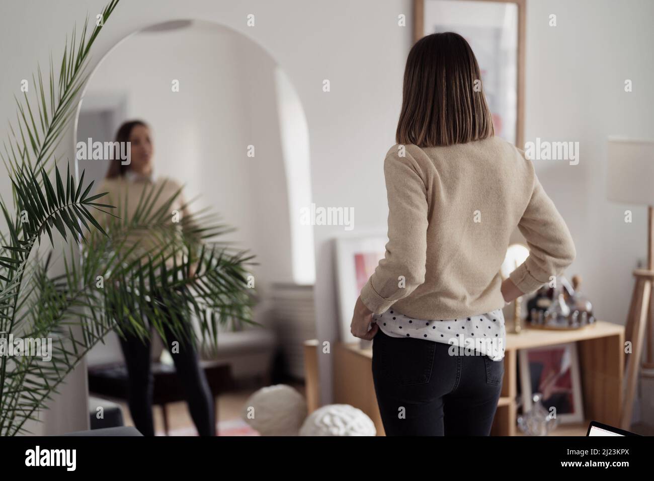 Self-confident Woman looking at her reflection into the mirror indoors ...