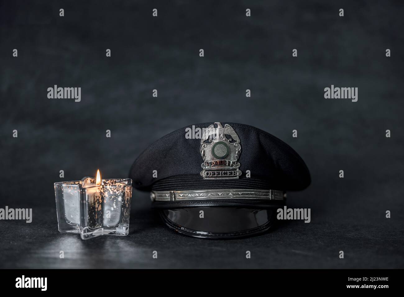 A black police hat cap in front of a navy blue background with a candle ...