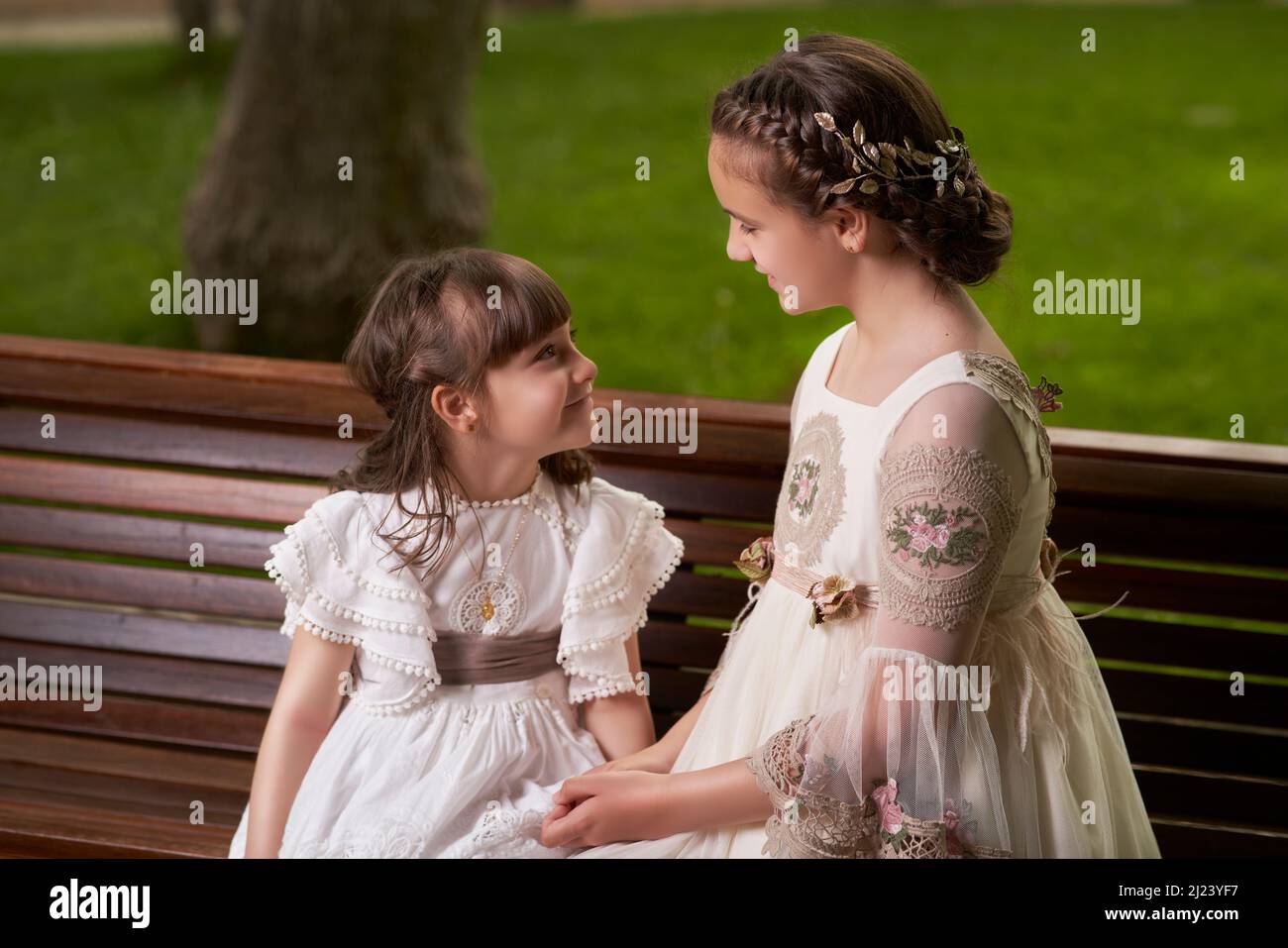 Communion girl posing with her sister sitting on park bench Stock Photo ...