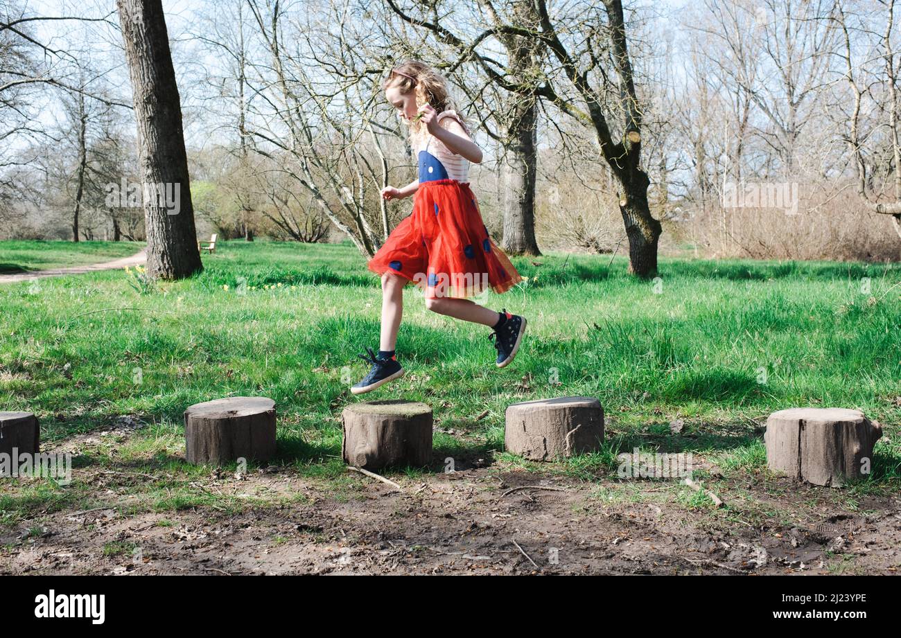 girl jumping on logs at the park in a dress Stock Photo - Alamy