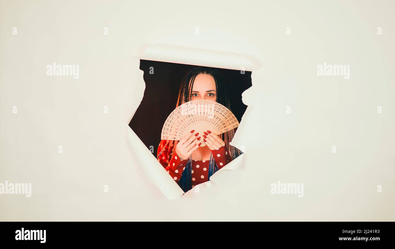 Young woman in red dress with fan in hole of white background in studio ...