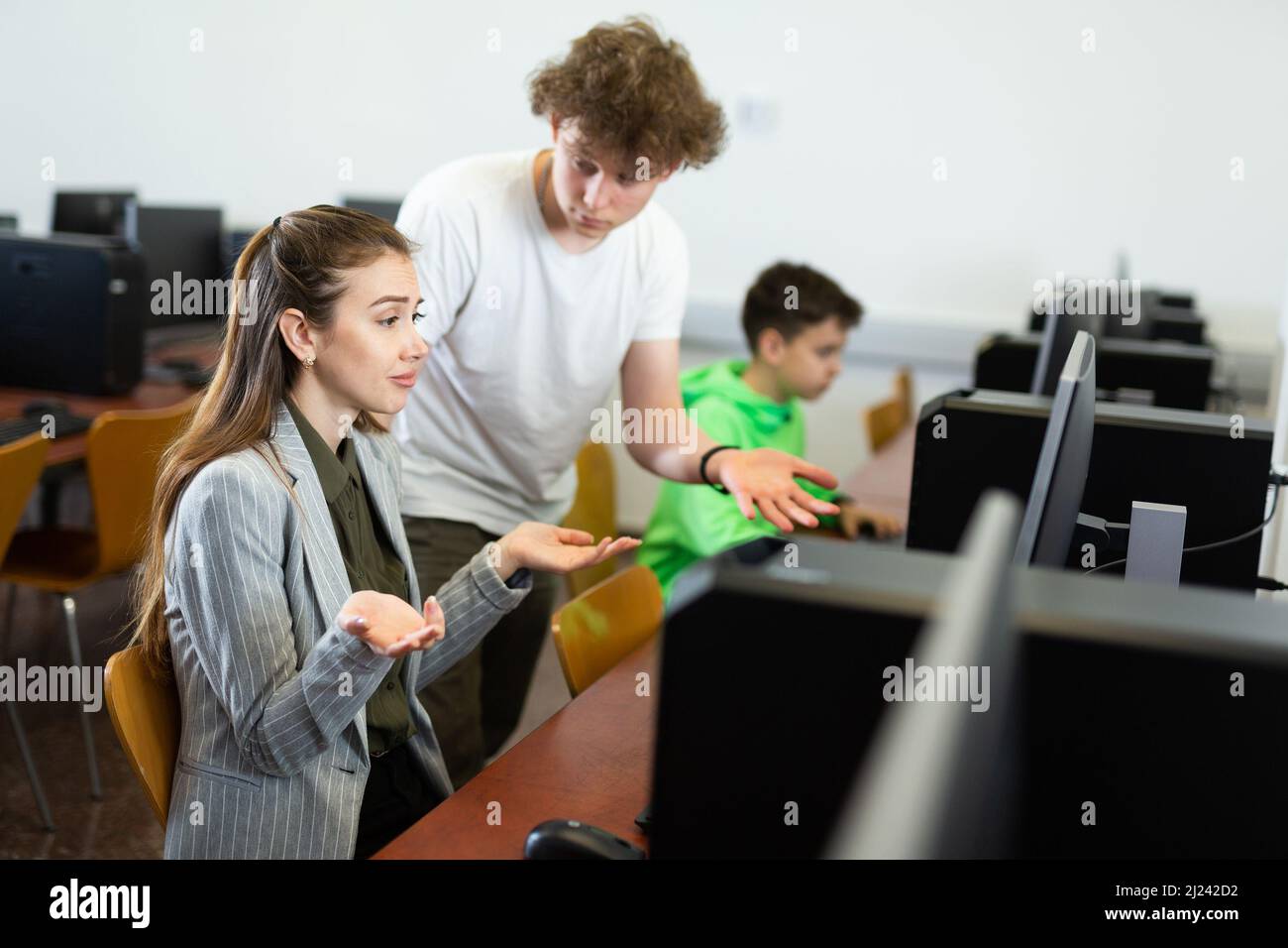 Teenage student helping young puzzled woman with computer in library ...