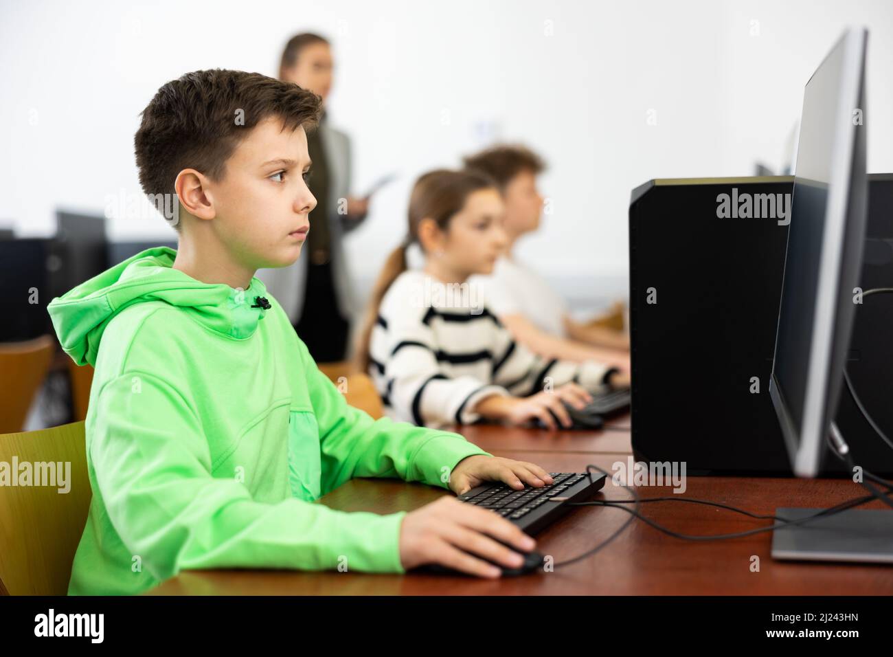 Schoolboy using computer at lesson, teacher teaching pupils in class ...