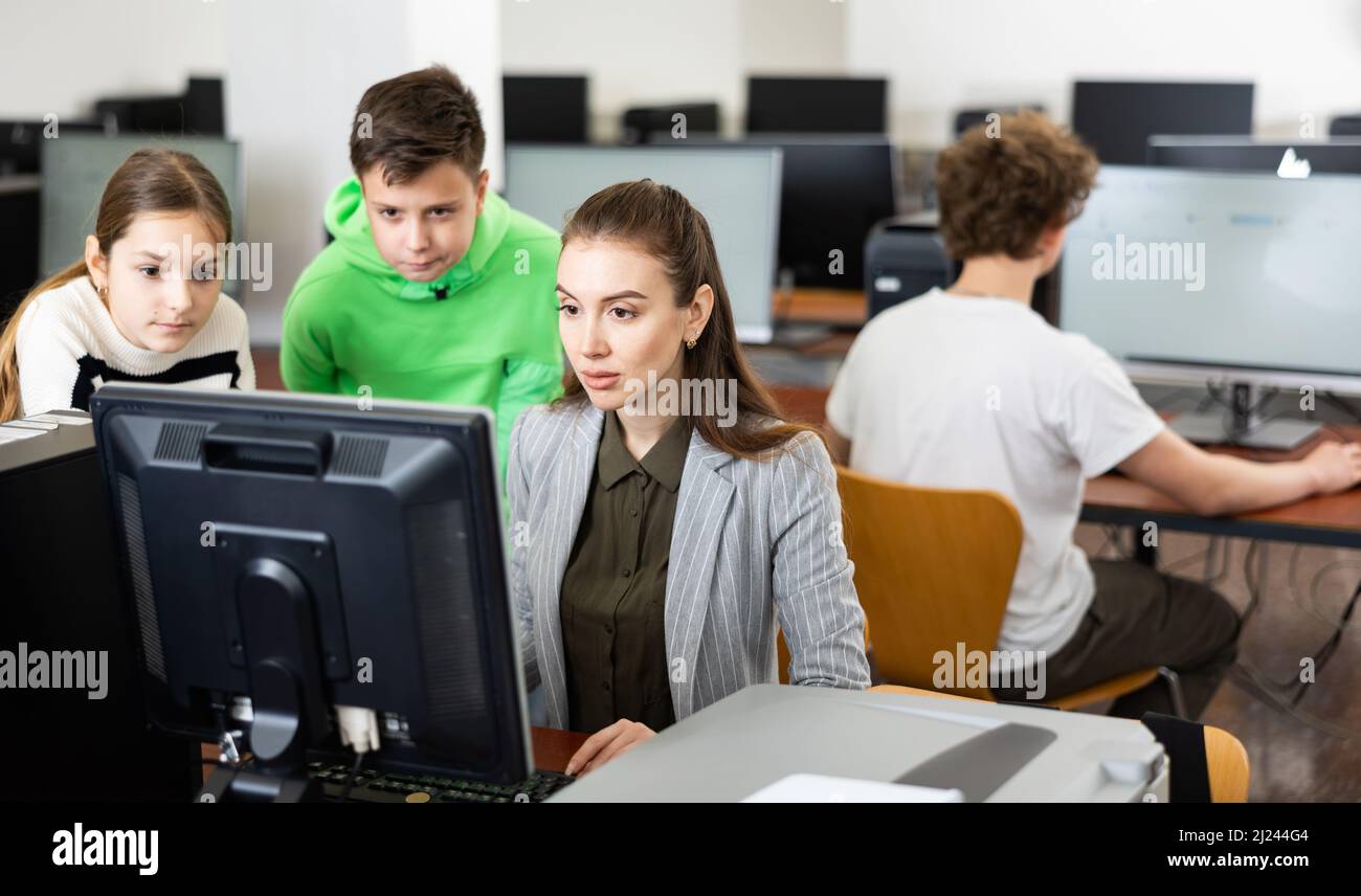 Female teacher and teen students looking at monitor screen during ...