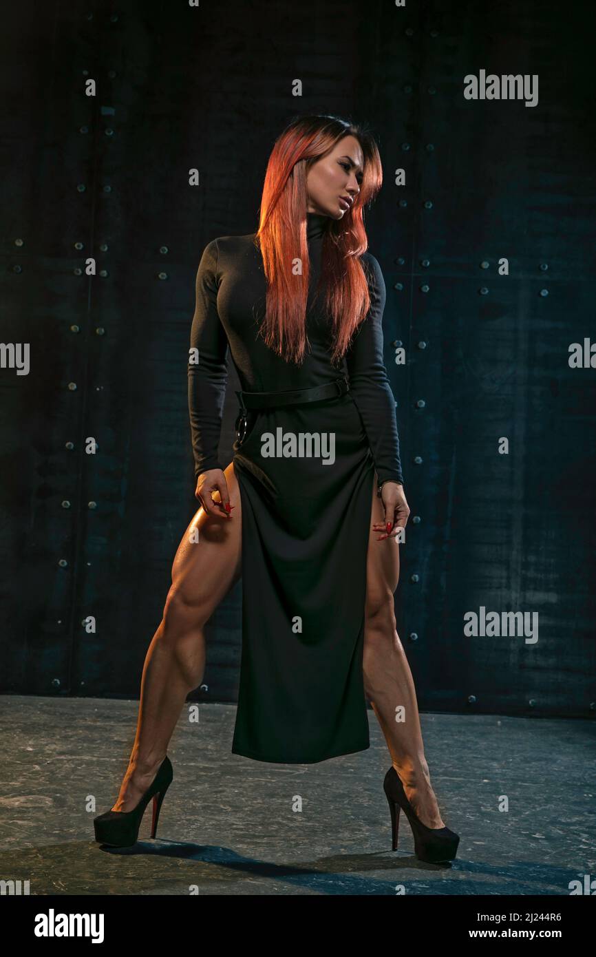 Attractive red-haired girl in black dress demonstrates athletic legs ...