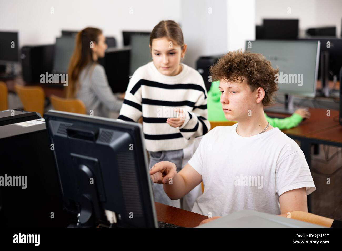 Teenager helps friend solve problem on computer in school class Stock ...
