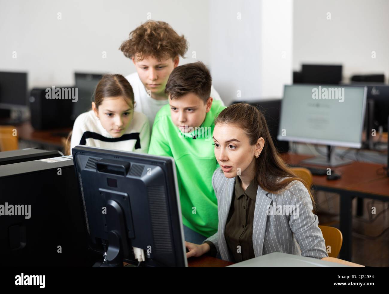 Female teacher and teenager pupils looking at monitor of PC Stock Photo ...