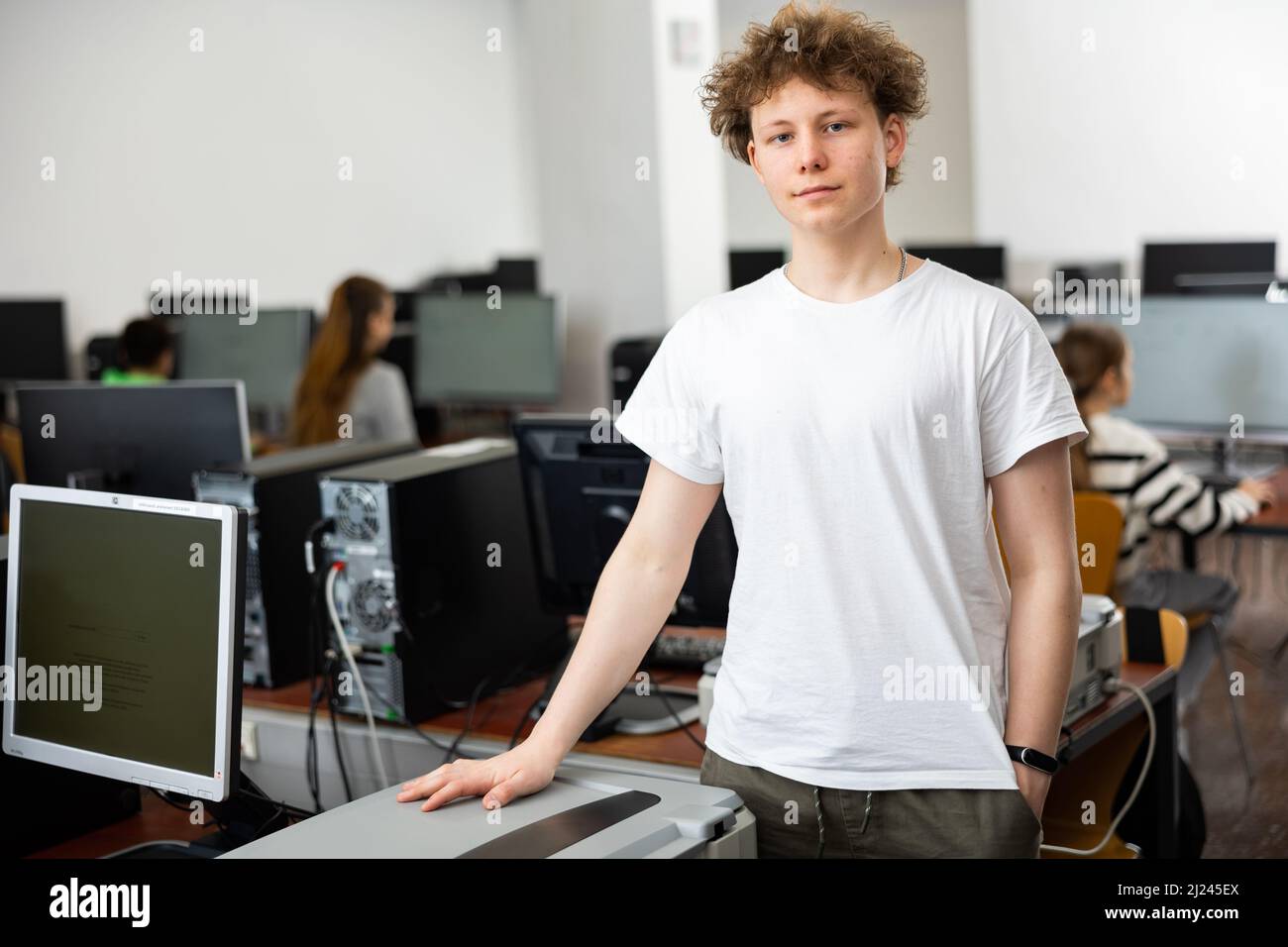 Confident teenage student standing in information technology classroom ...