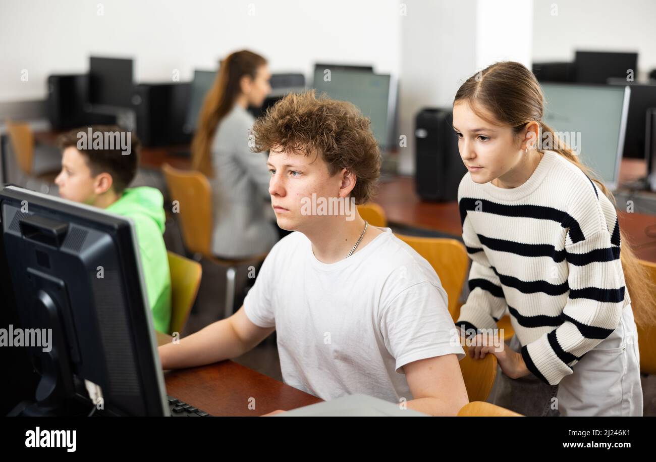 Teen schoolgirl talking to focused classmate in computer class Stock ...