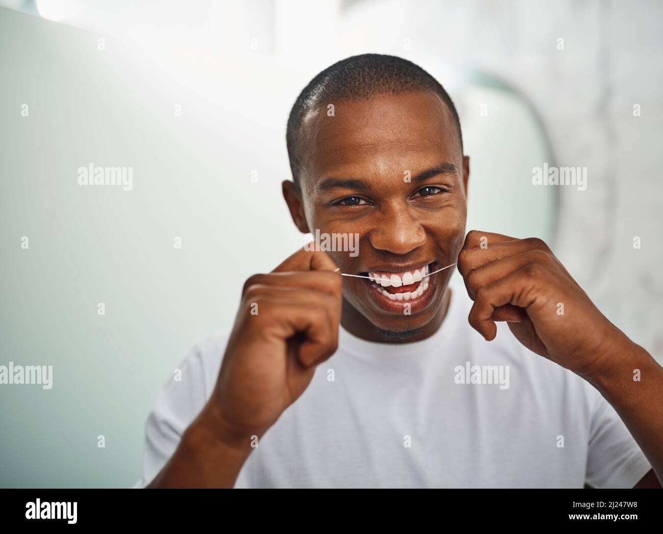 Reaching those areas my toothbrush cant. Portrait of a handsome young man flossing his teeth in ...