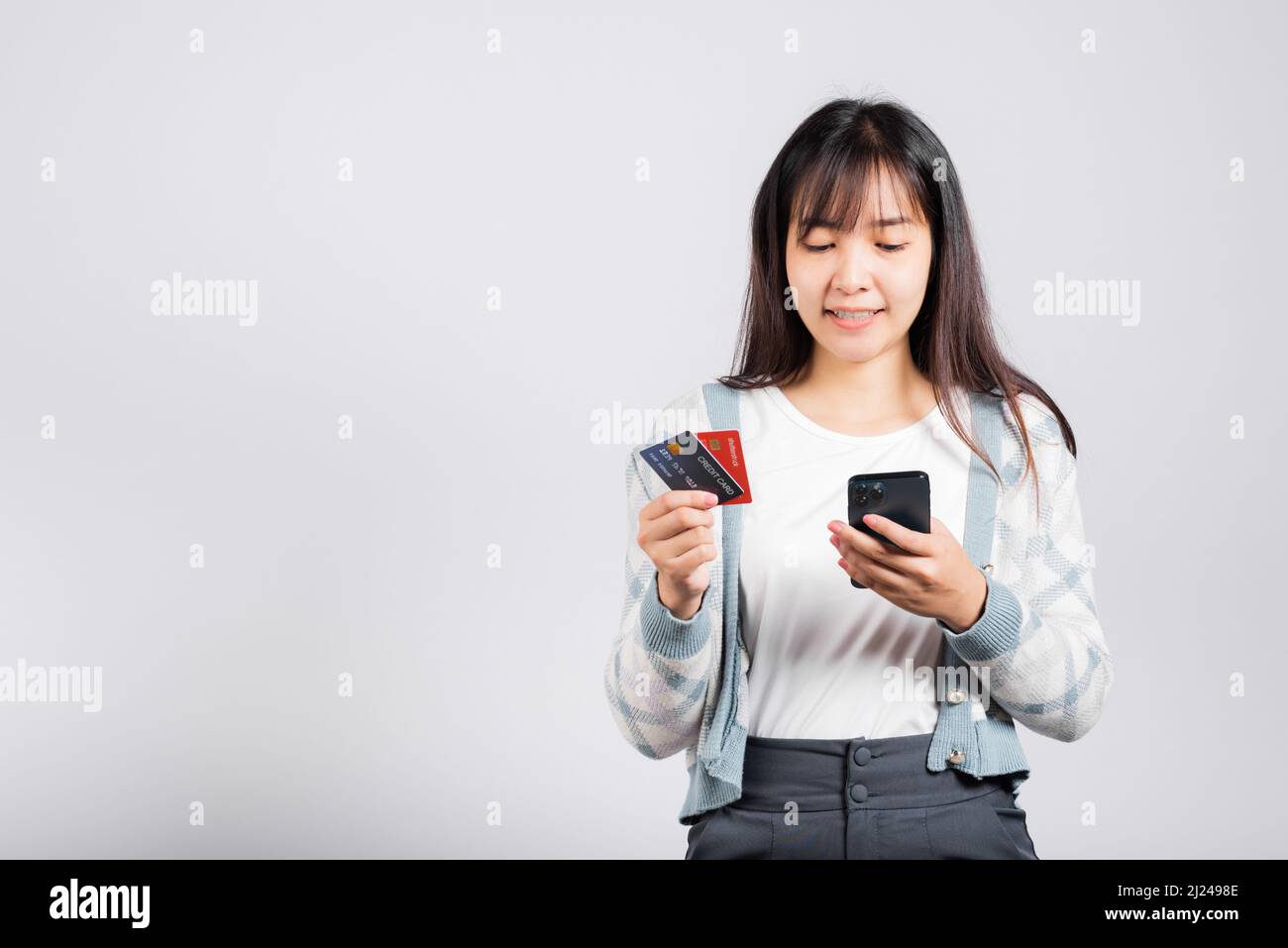 Woman excited smiling hold mobile phone and plastic debit credit bank card for payment studio ...