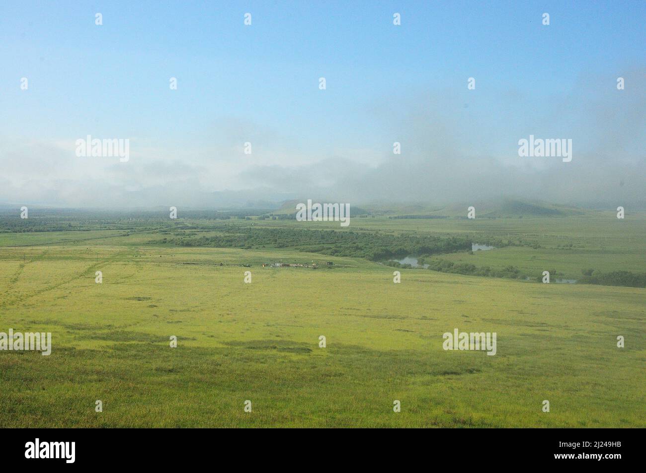 A flat huge steppe with a flowing river and mountains covered by clouds ...