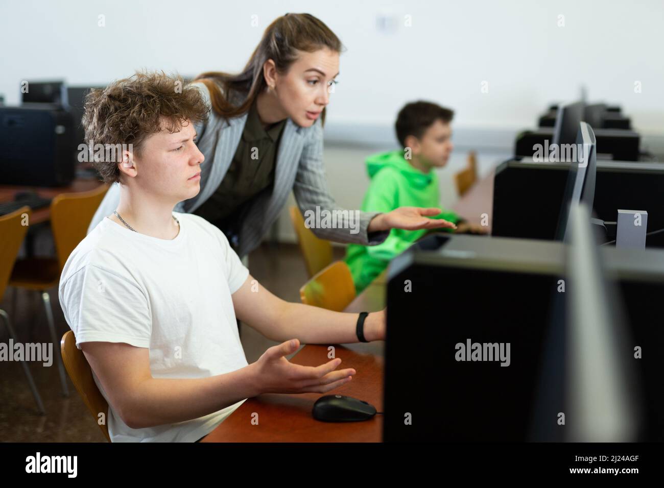 Female teacher helping focused teenage student in computer lab Stock ...