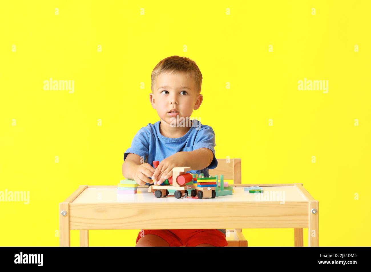 Cute little boy playing with building blocks at table on yellow ...