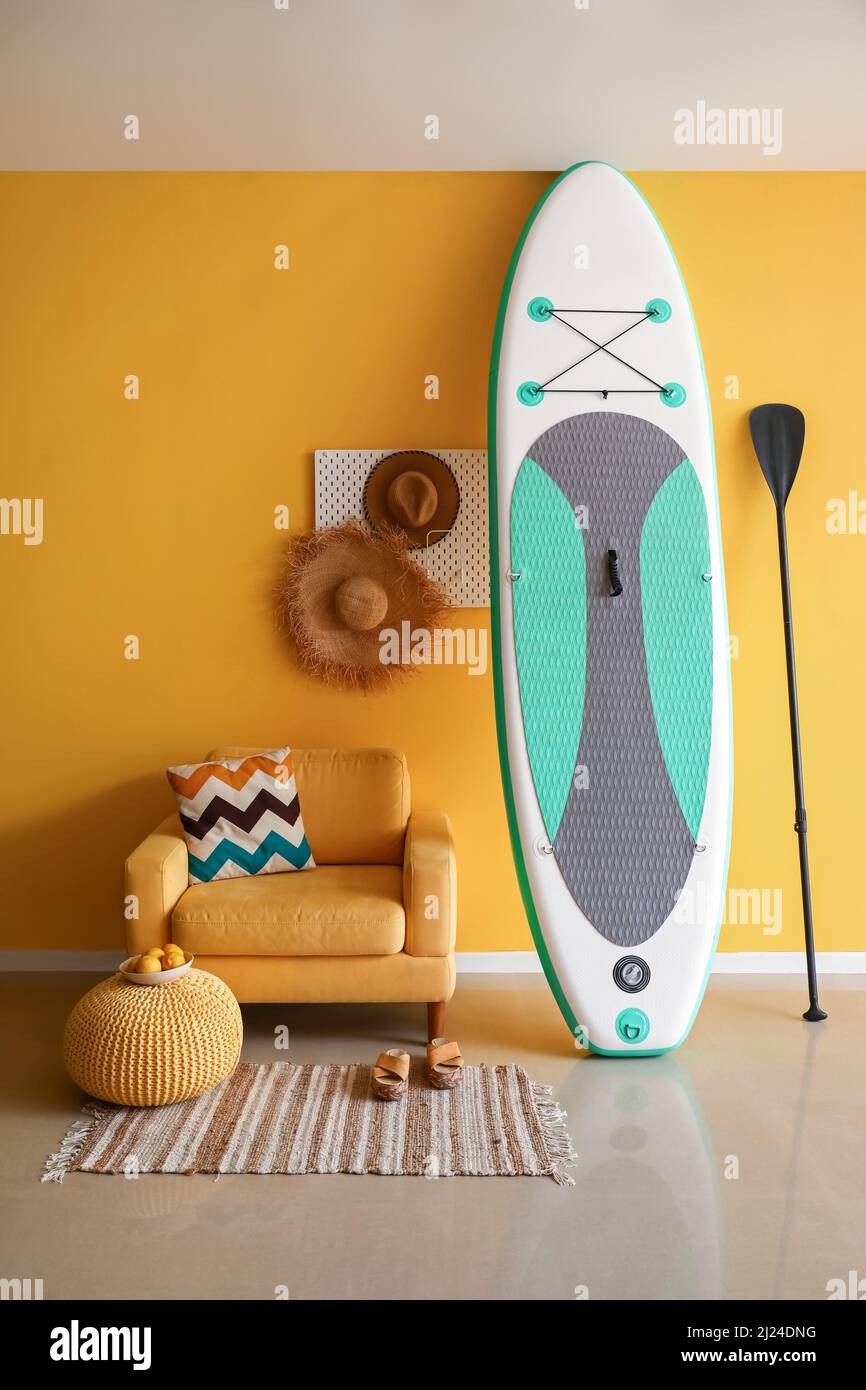 Interior of room with armchair and board for sup surfing near yellow ...