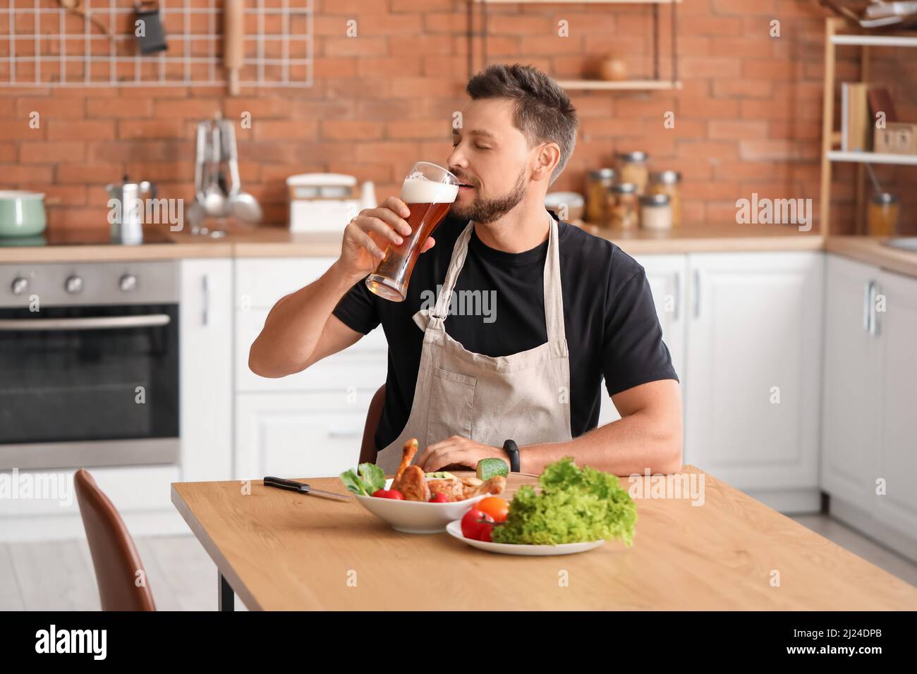 Handsome man drinking beer while having lunch in kitchen Stock Photo ...