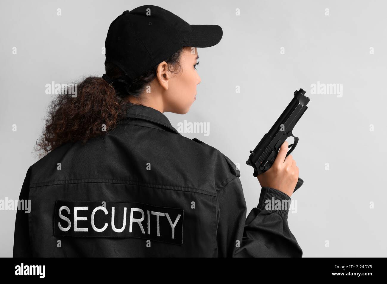 African-American female security guard with gun on light background ...