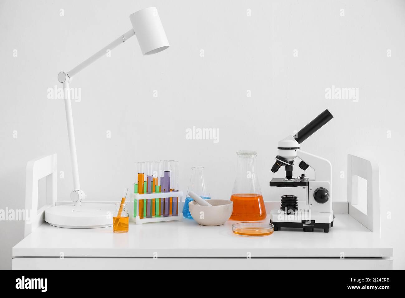 Table with lamp, chemical glassware and microscope near light wall ...