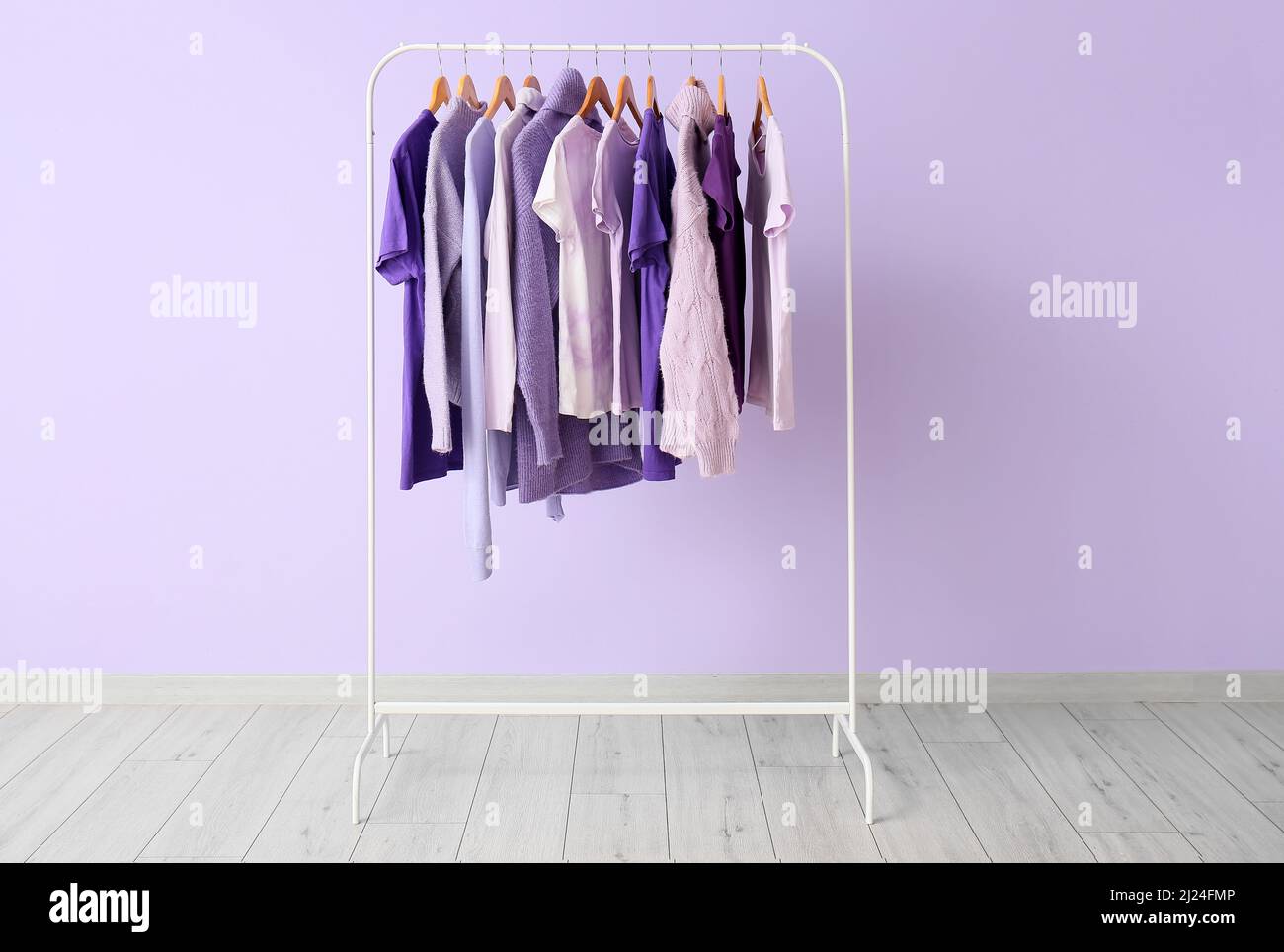 Rack with clothes in purple shades near lilac wall Stock Photo - Alamy