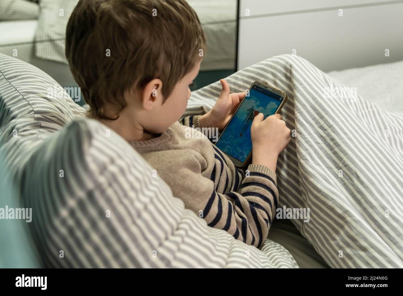 Boy playing game on smartphone comfortably sitting on the bed Stock ...