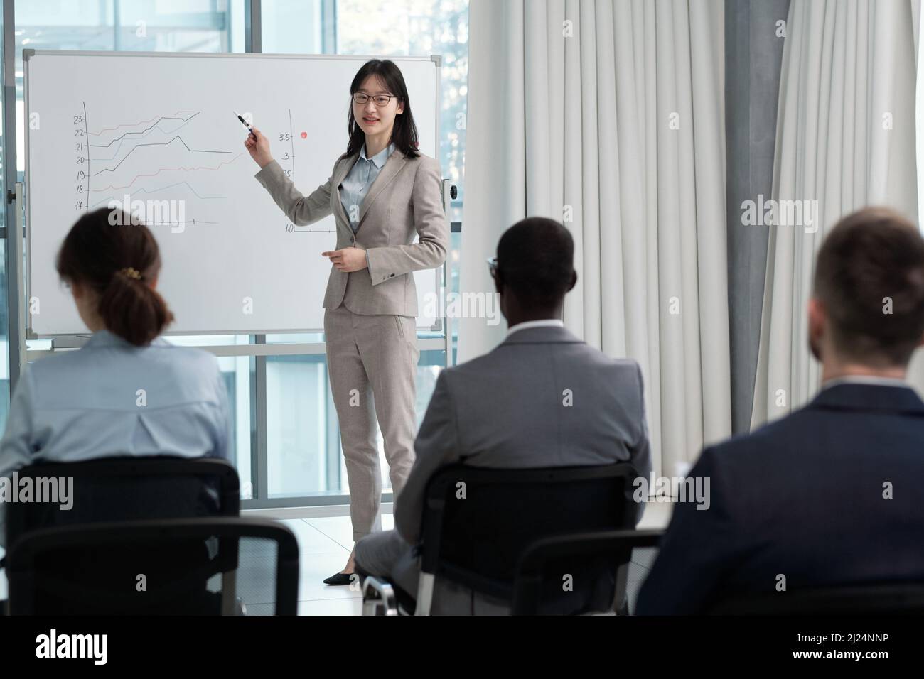 Successful business coach pointing at graphs on whiteboard at seminar ...