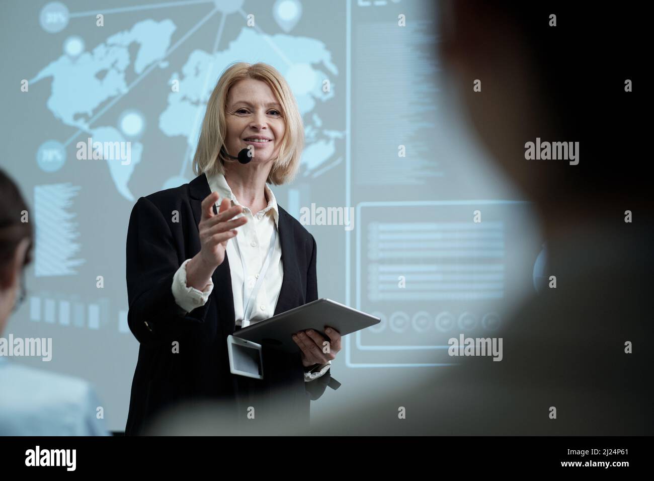 Happy mature female lecturer with tablet speaking to one of colleagues ...